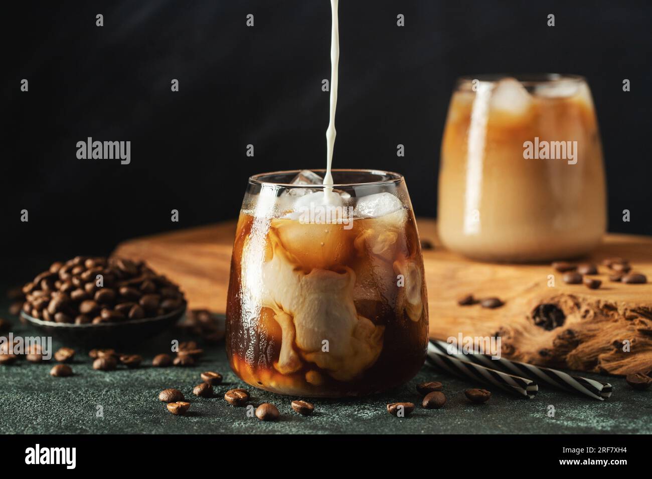 Ice coffee in a tall glass with cream poured over, ice cubes and beans ...