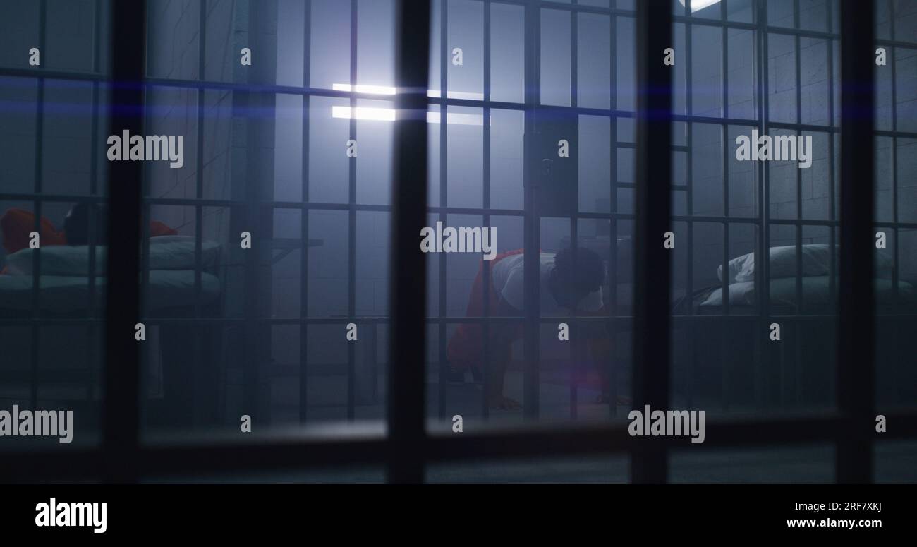 African American prisoner in orange uniform does push-ups and shadow ...