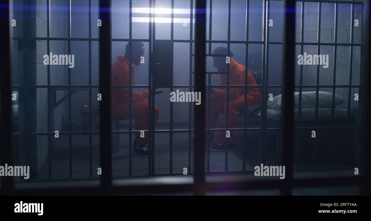 African American prisoners in orange uniforms sit on jail beds and ...