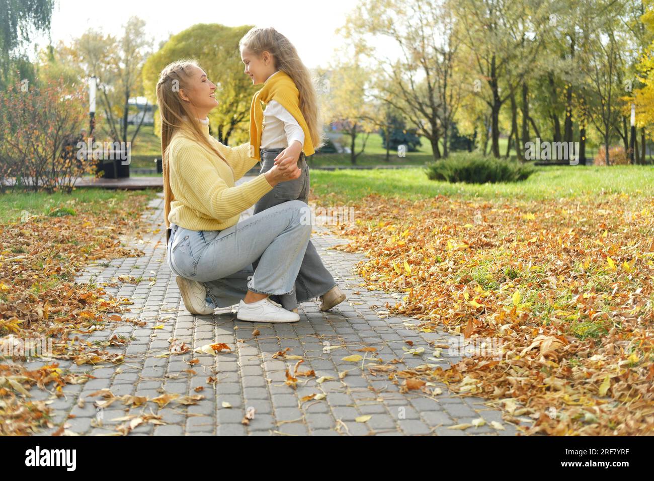 young blonde mother kneeling and hugging the girl daughter in the park ...