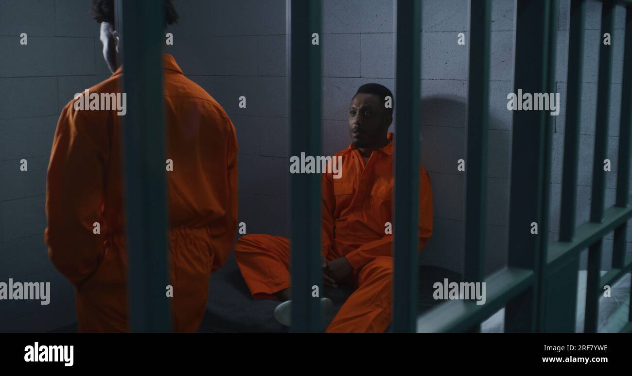 Two African American prisoners in orange uniforms talk. One man sits on ...