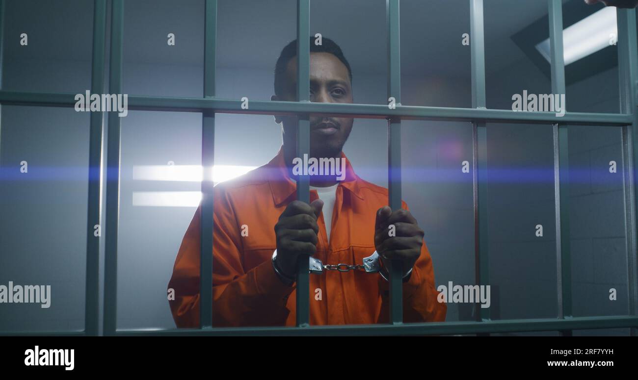 African American prisoner in orange uniform keeps hands in handcuffs on ...