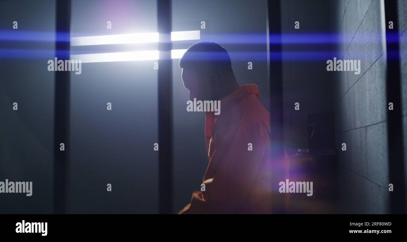 Depressed African American man in orange uniform stands from jail bed ...