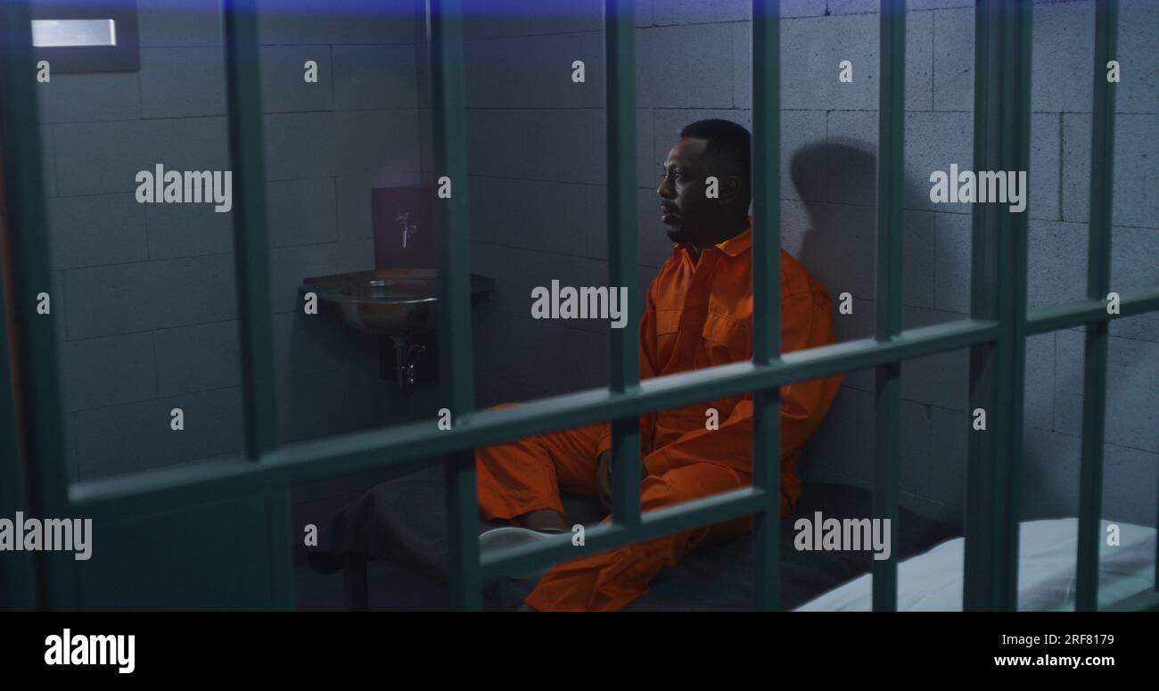 African American man sits on the bed and talks with criminal in prison ...