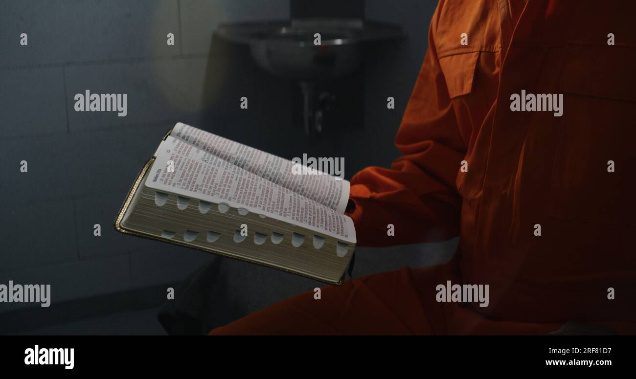 African American prisoner in orange uniform reads Bible in prison cell ...