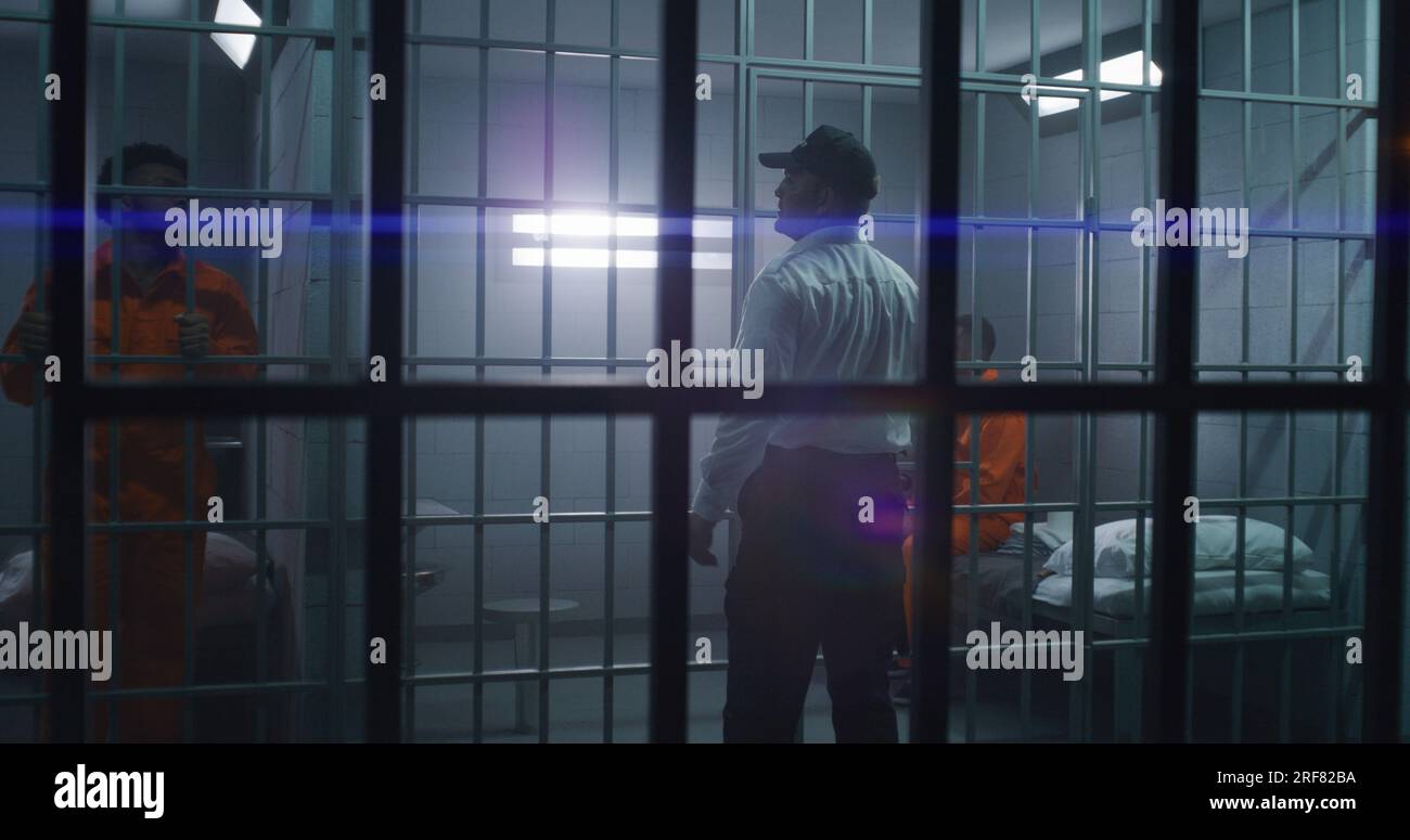 Jailer with police baton stands in front of jail cells and talks with ...