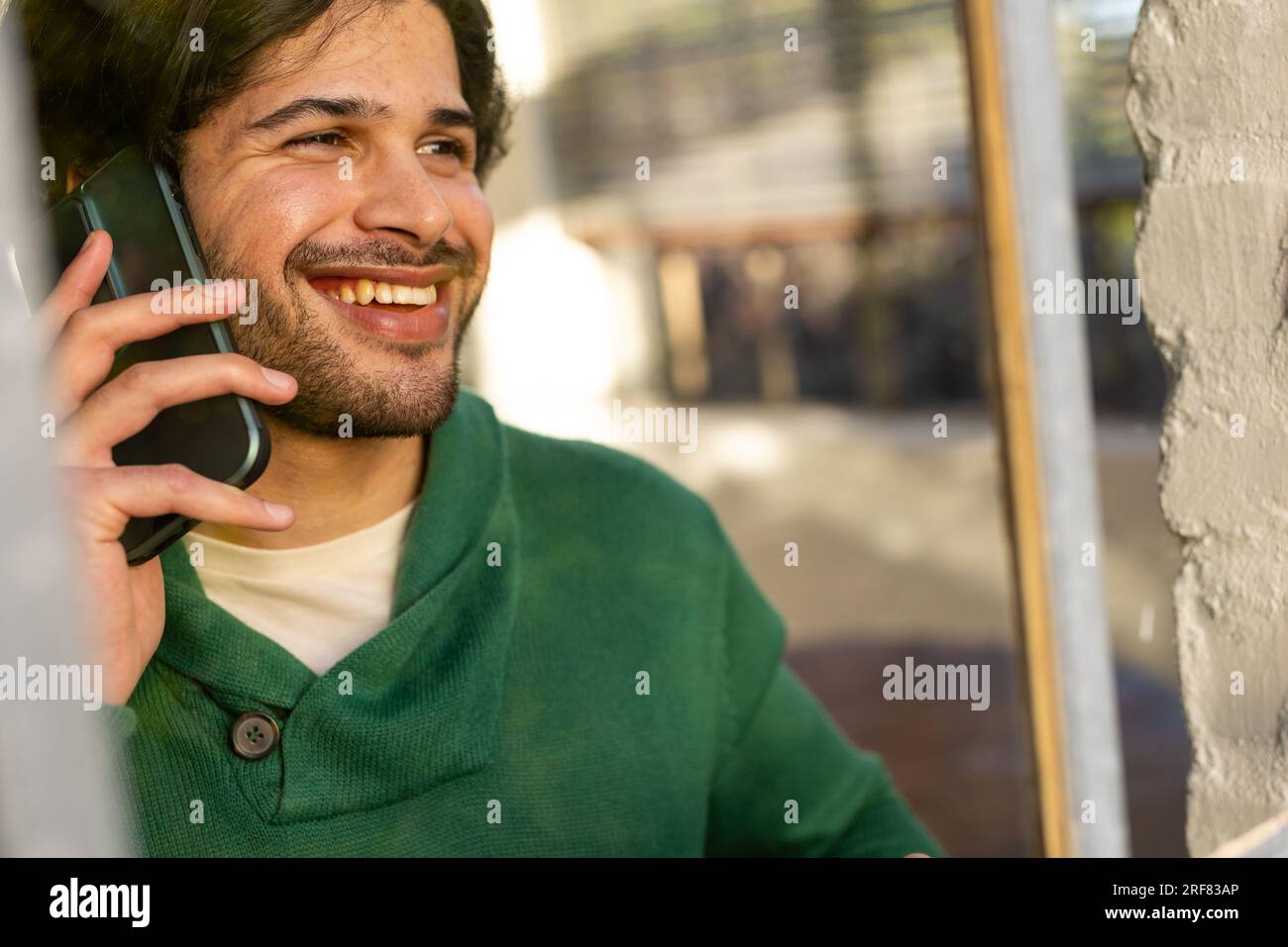 Happy indian man talking on smartphone and looking out window at home ...