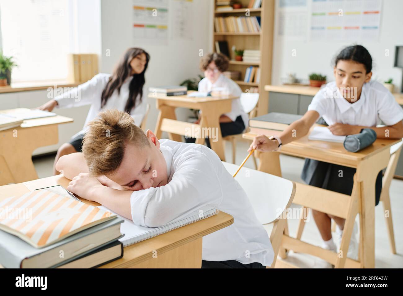 Schoolboy sleeping at desk at lesson while his classmate waking him up ...
