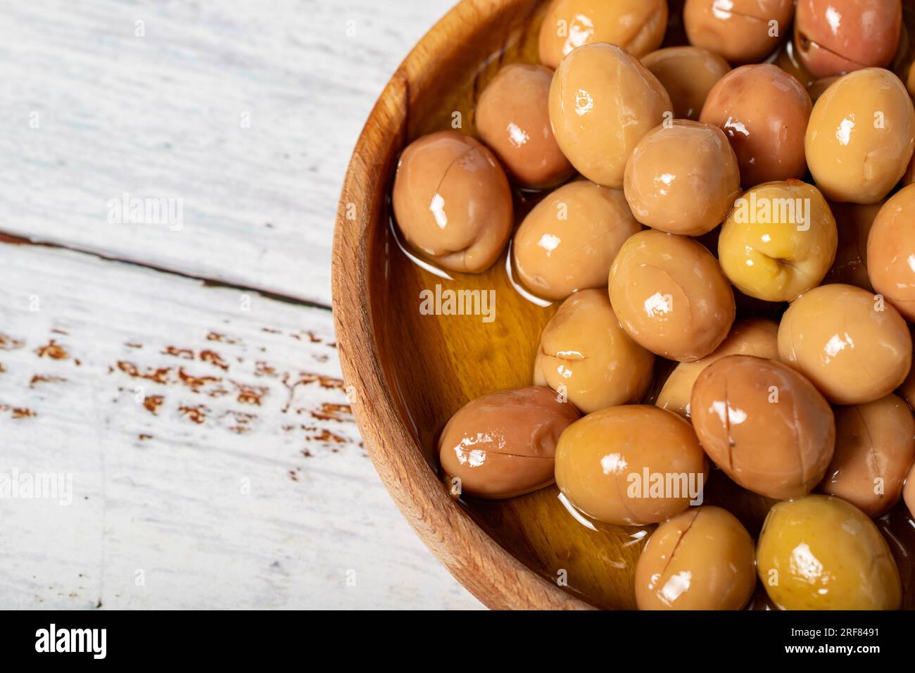 Scratched green olive at wooden bowl. Green olives on a white wood ...