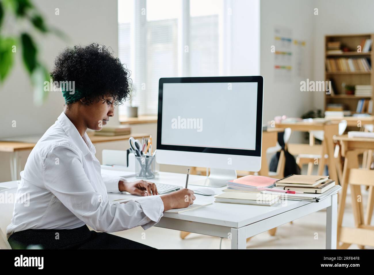 African American teacher sitting at her workplace with computer in ...