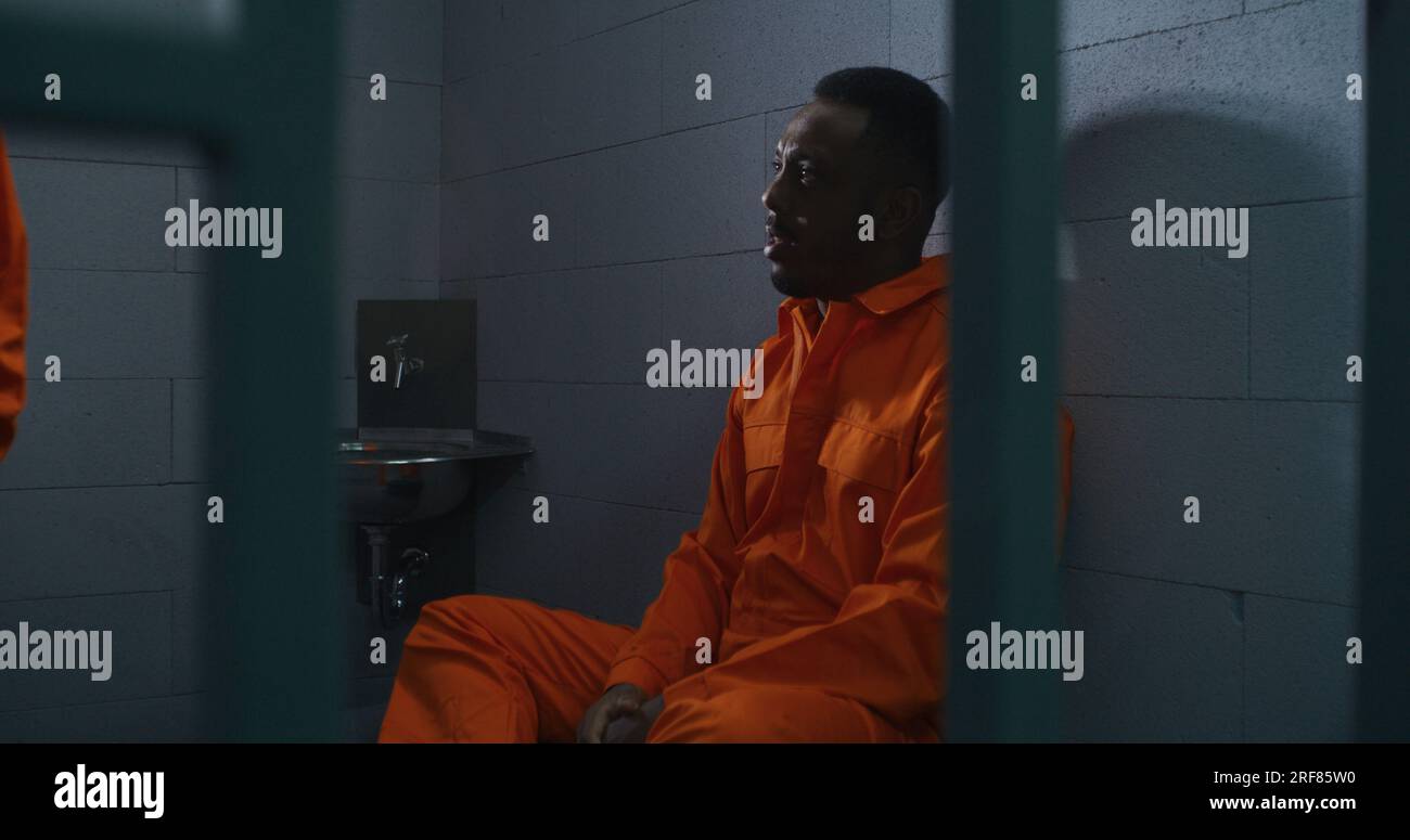 African American man sits on the bed and talks with criminal in prison ...