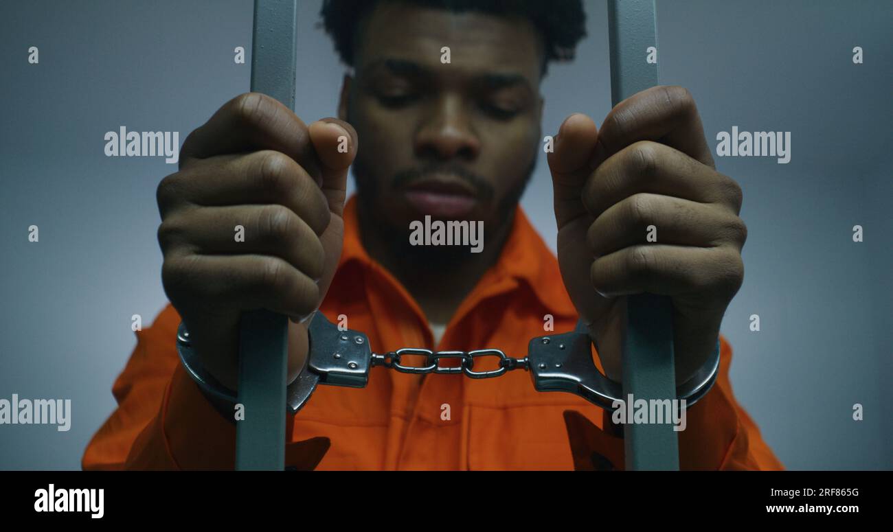 African American prisoner in orange uniform keeps hands in handcuffs on ...