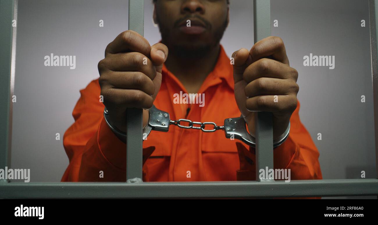 African American prisoner in orange uniform keeps hands in handcuffs on ...