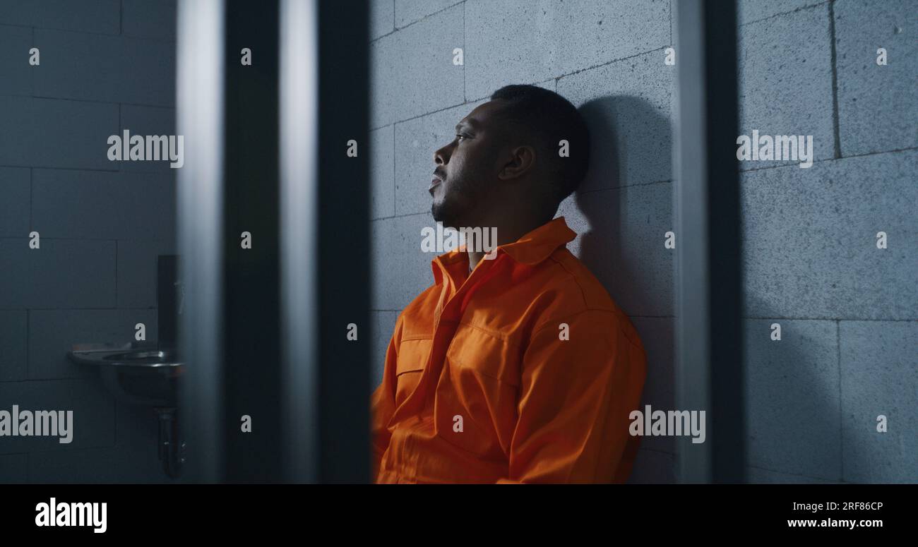 Guilty African American man in orange uniform sits on prison bed and ...