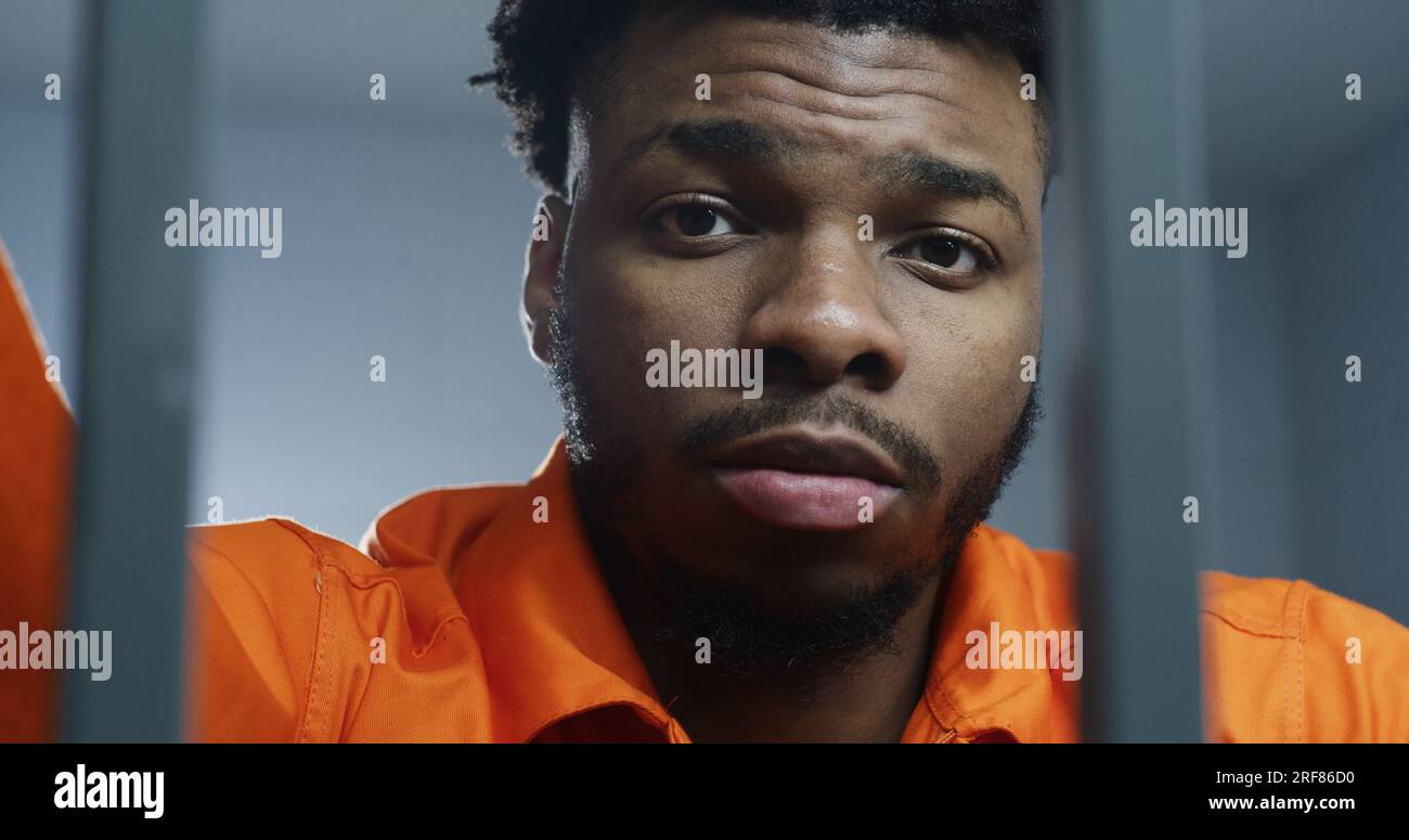 African American man in orange uniform stands behind prison cell bars ...