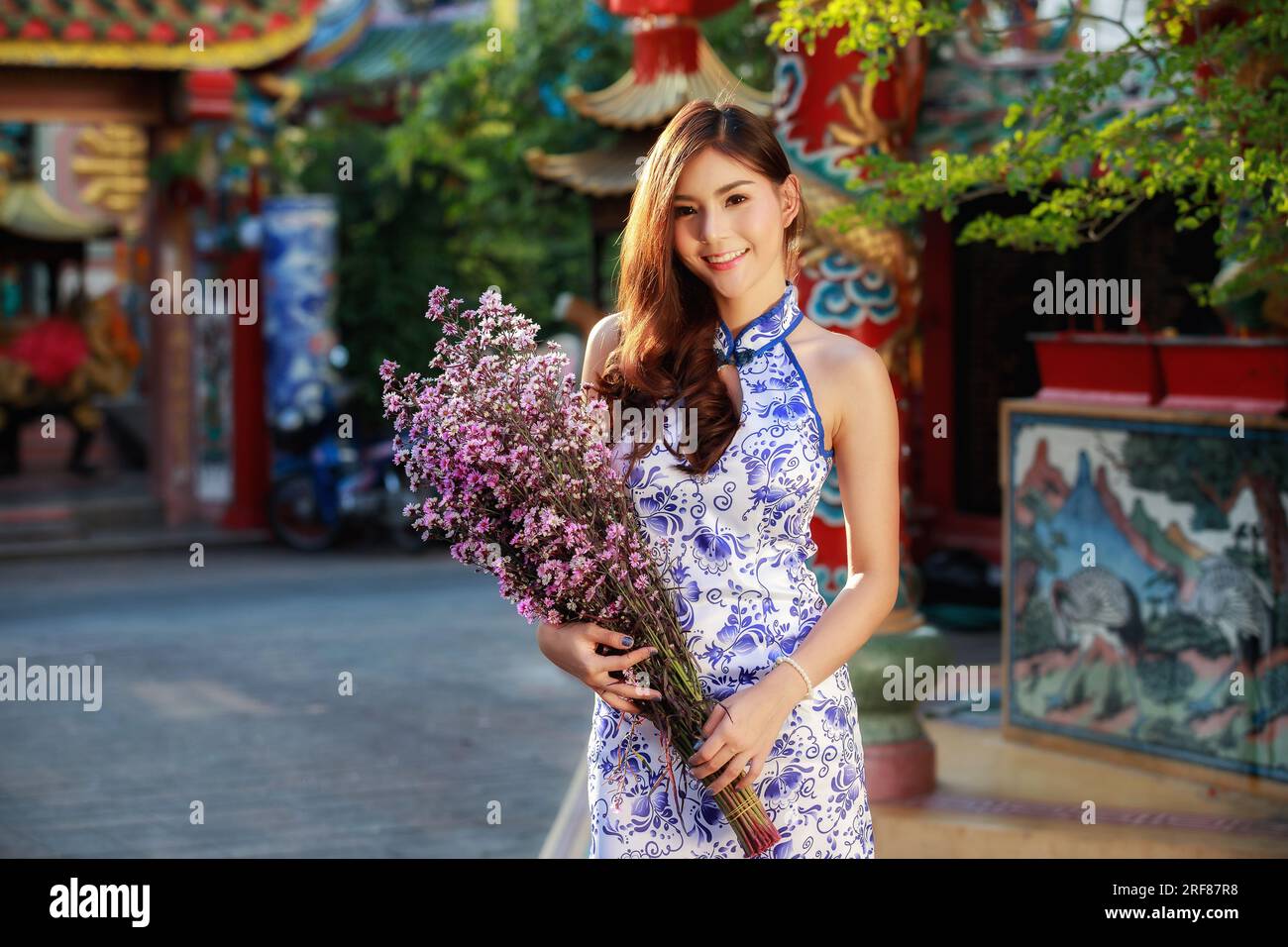 Chinese woman in cheongsam dress with a bouquet of flowers at shrine ...