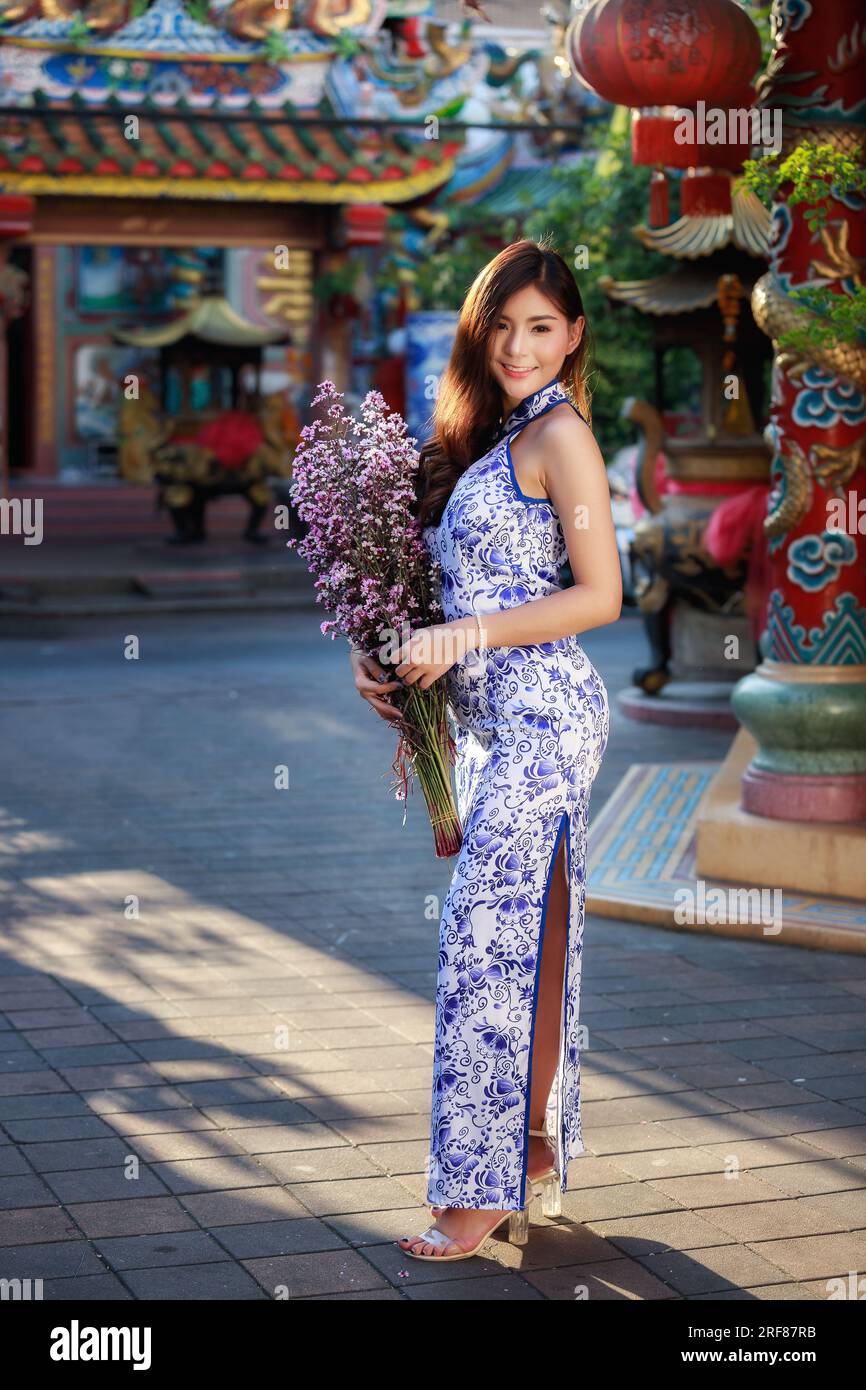 Chinese woman in cheongsam dress with a bouquet of flowers at shrine ...