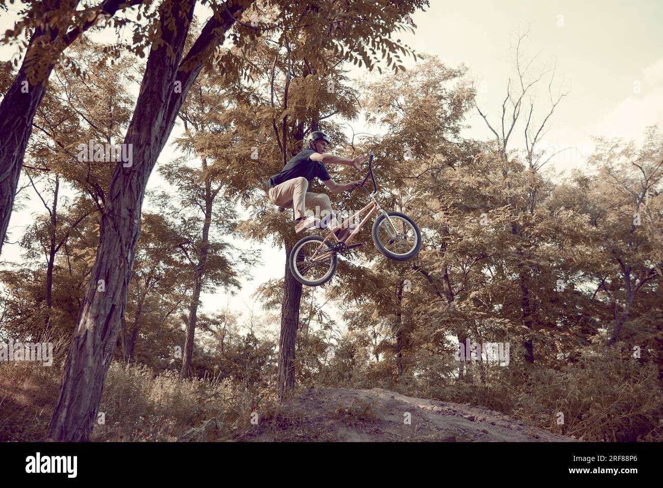 Young man in helmet training outdoors in forest, riding bmx bike, doing ...