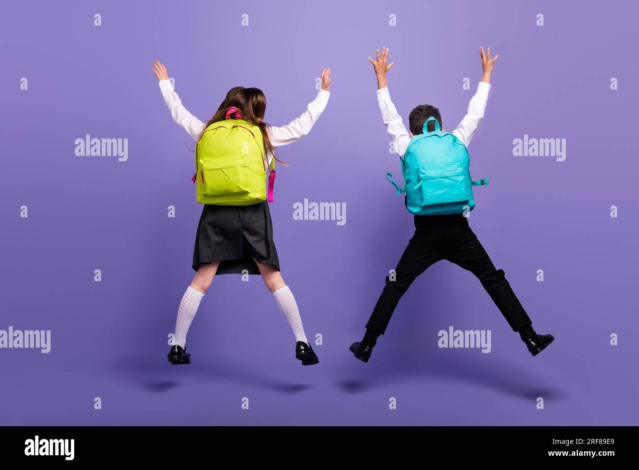 Back rear spine photo of two school kids jumping with new backpacks for ...