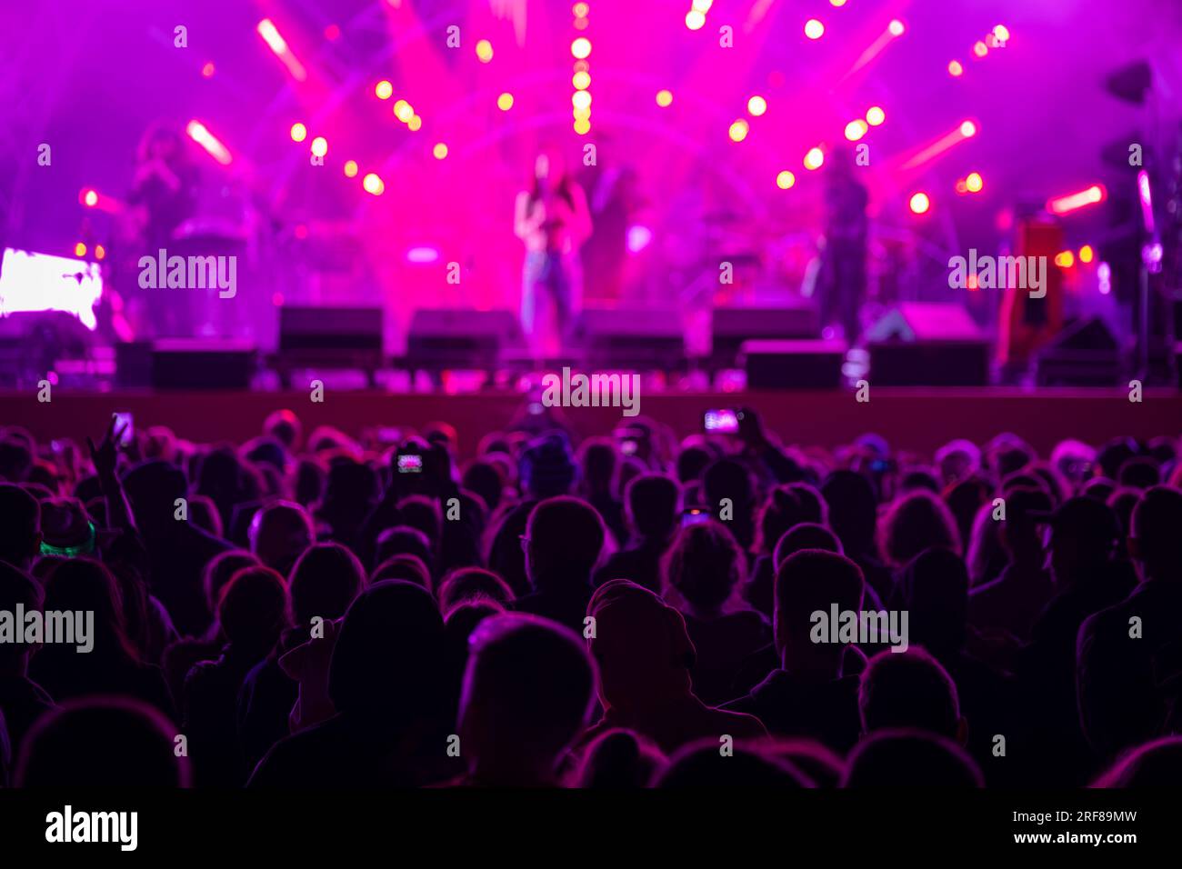 Crowd of fans near stage with performing music band in glowing red ...
