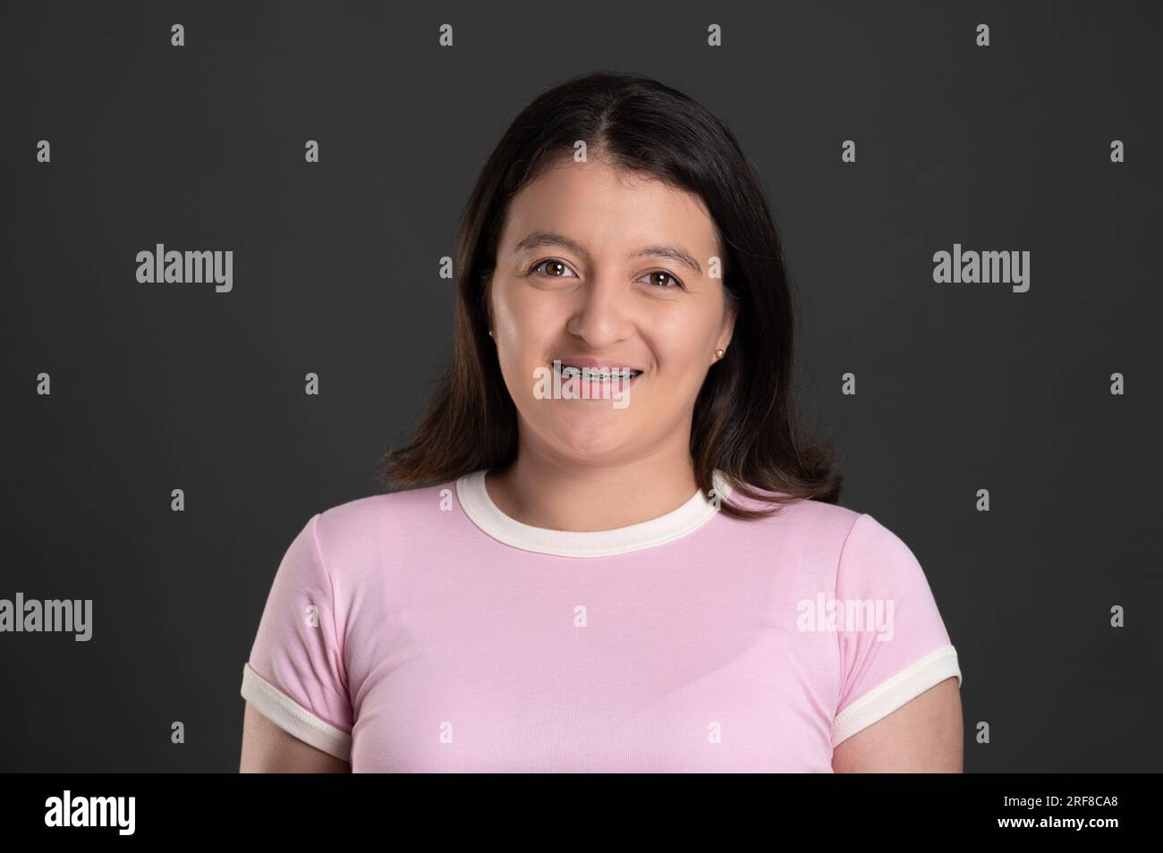 Portrait of hispanic girl with teeth brackets on dark gray studio ...