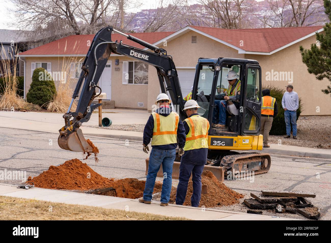 A utility worker uses a track hoe to excavate a hole in the street to ...