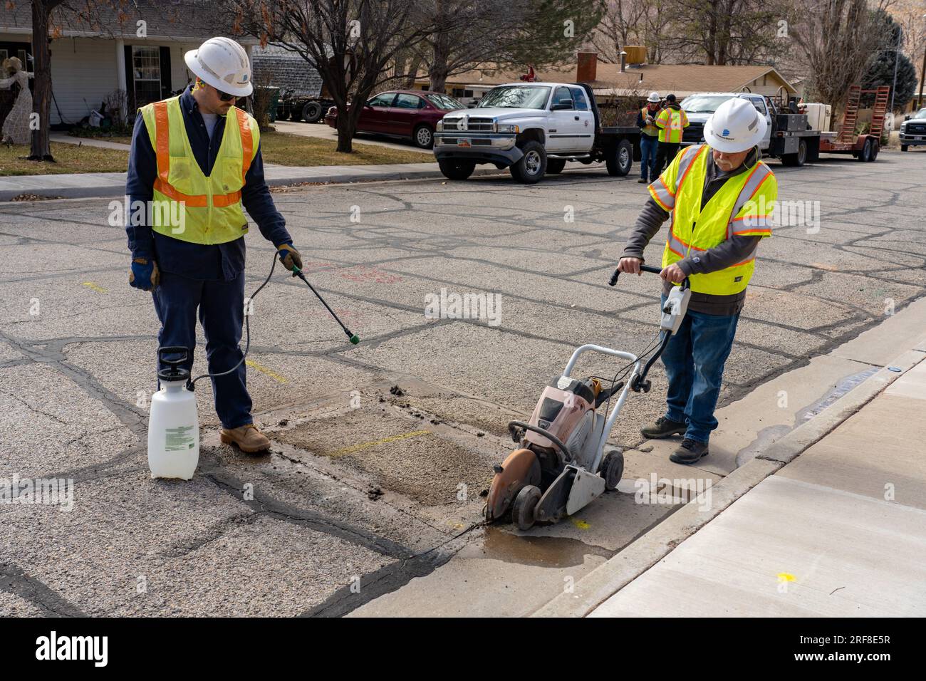 Utility workers use a saw to remove a section of pavement to repair a ...