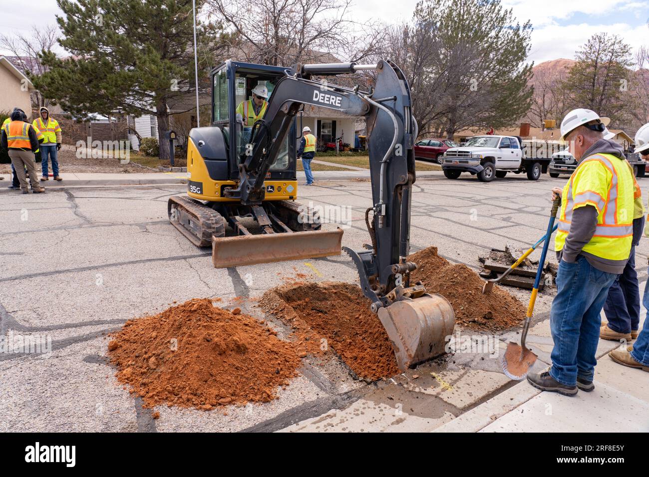 A utility worker uses a track hoe to excavate a hole in the street to ...