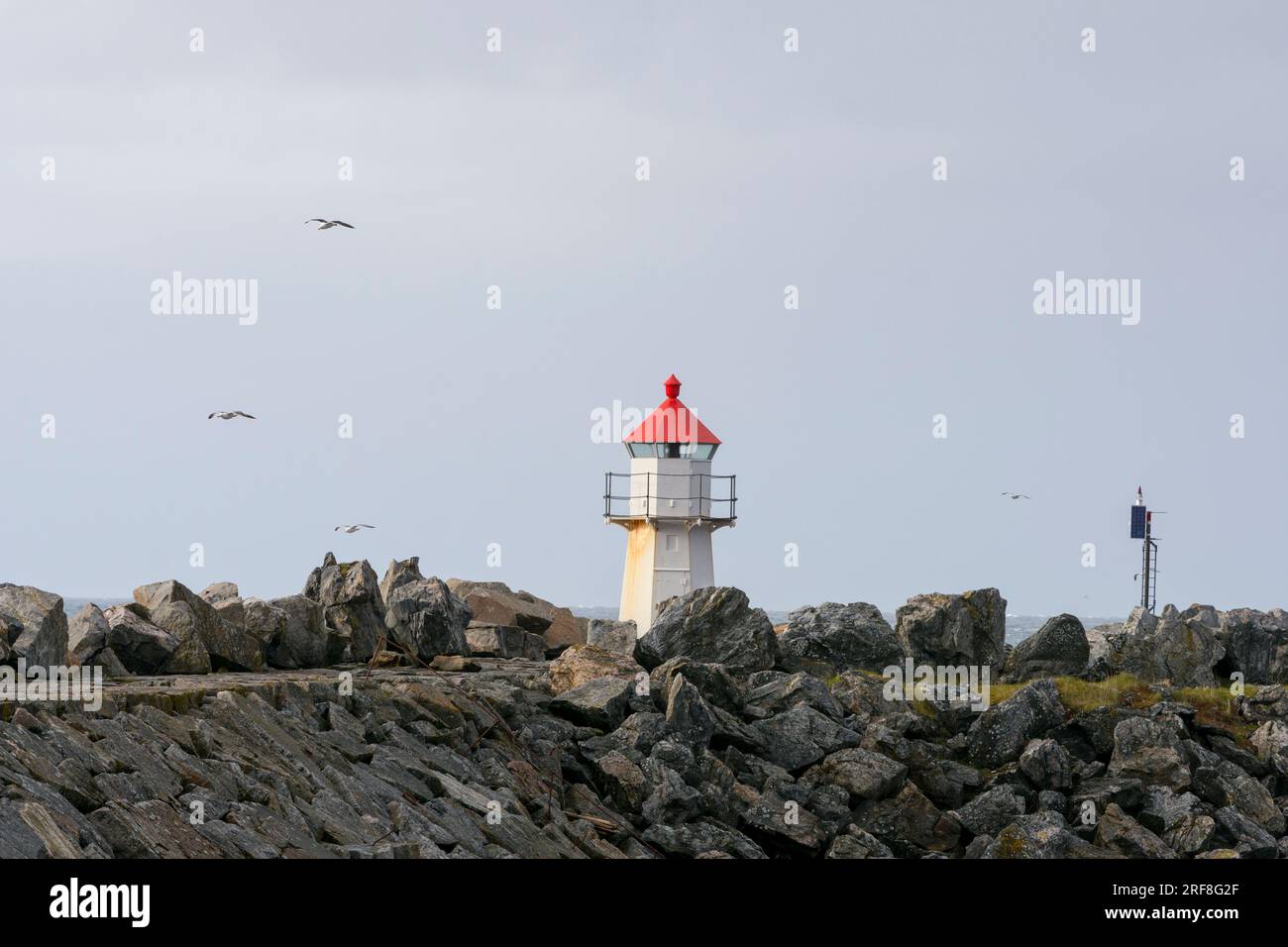 Small white and red lighthouse at the end of a quay wall against the ...