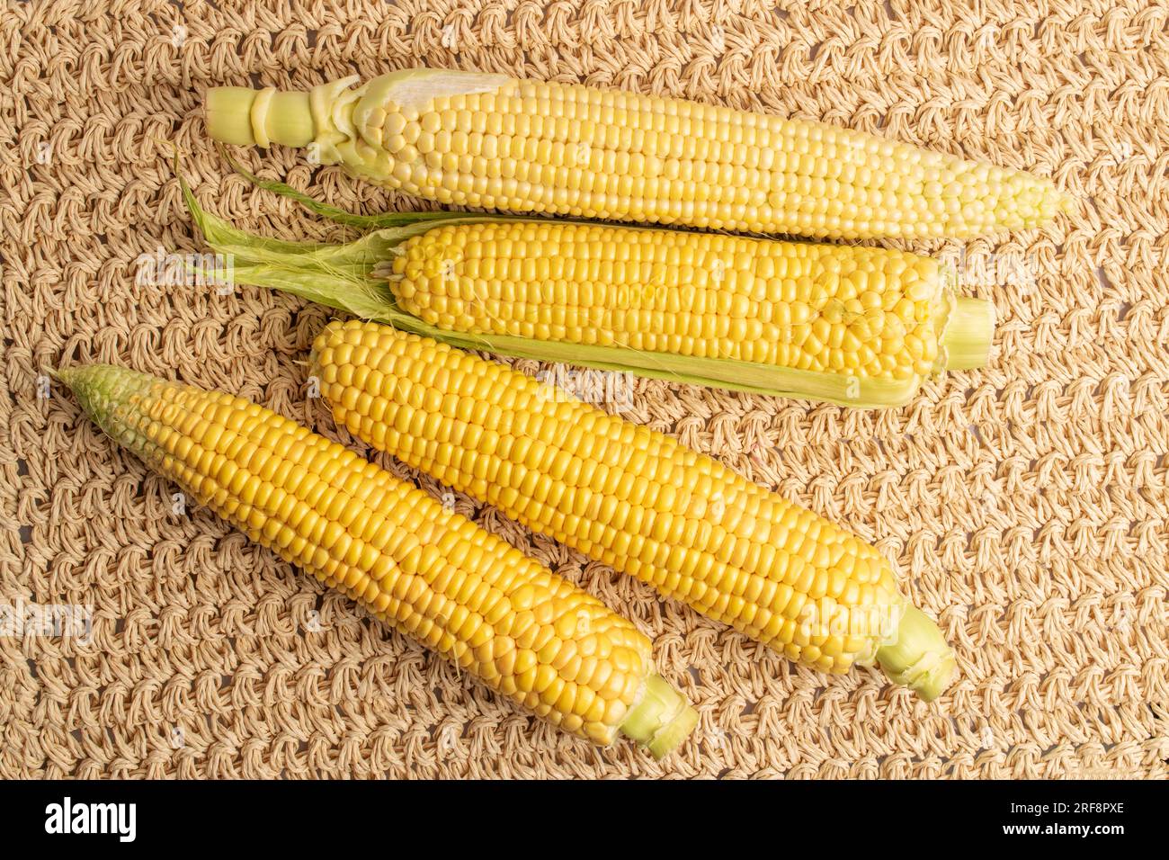 Four cobs of organic sweet corn on a straw mat, close-up, top view ...