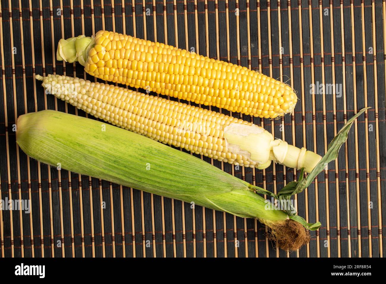 Three cobs of sweet organic corn, close-up, on a bamboo mat, top view ...