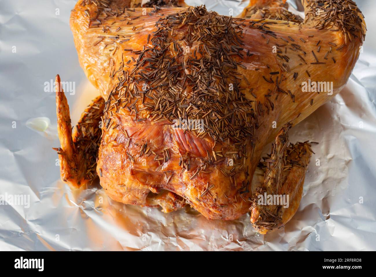 Whole roat chicken, covered in rosemary, on aluminium kitchen foil ...