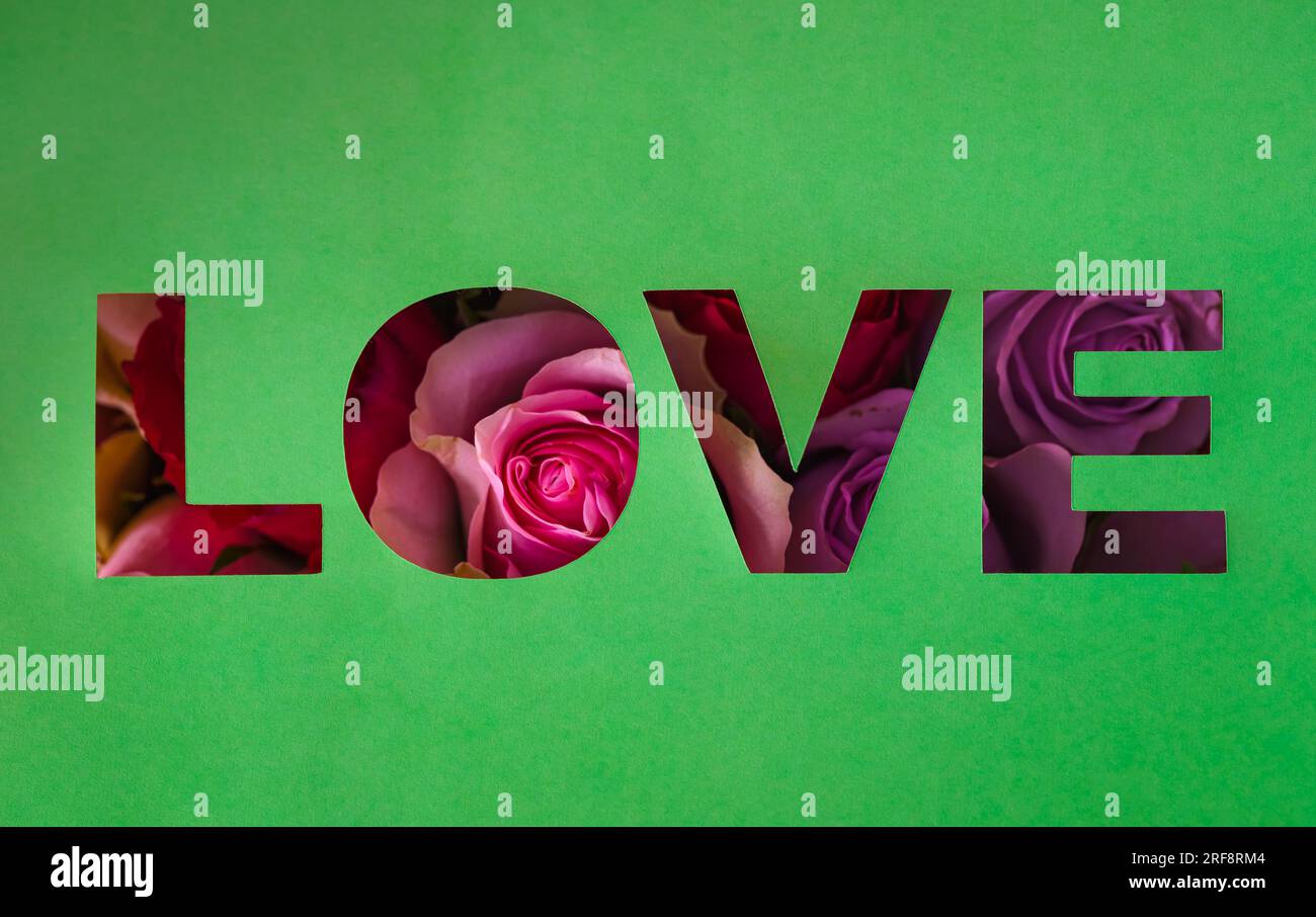 The word Love cut out of a green piece of paper with roses visible ...