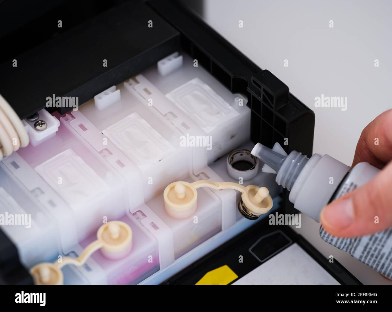 Person hand holding the bottle with black colour ink refilling printer ...