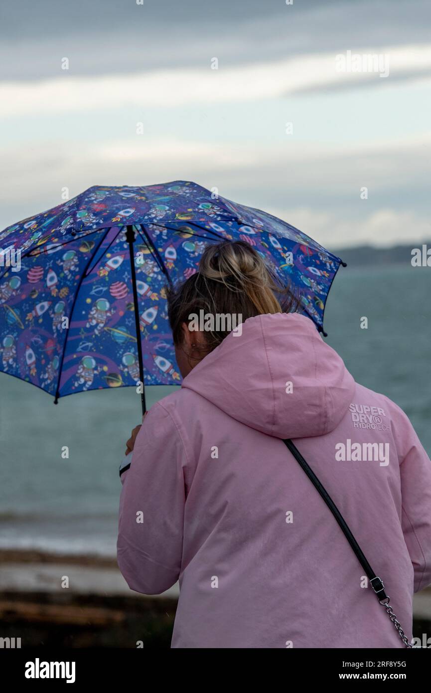 woman using colourful umbrella to shelter from the rain on a wet day at ...