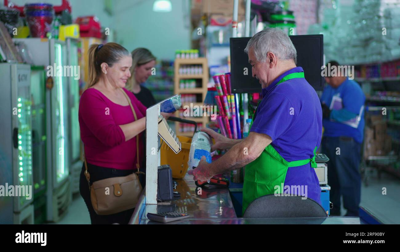 Senior employee at cashier scanning products at checkout, customers ...