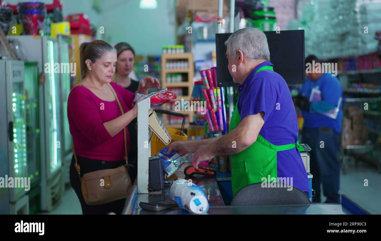 Senior employee at cashier scanning products at checkout, customers ...