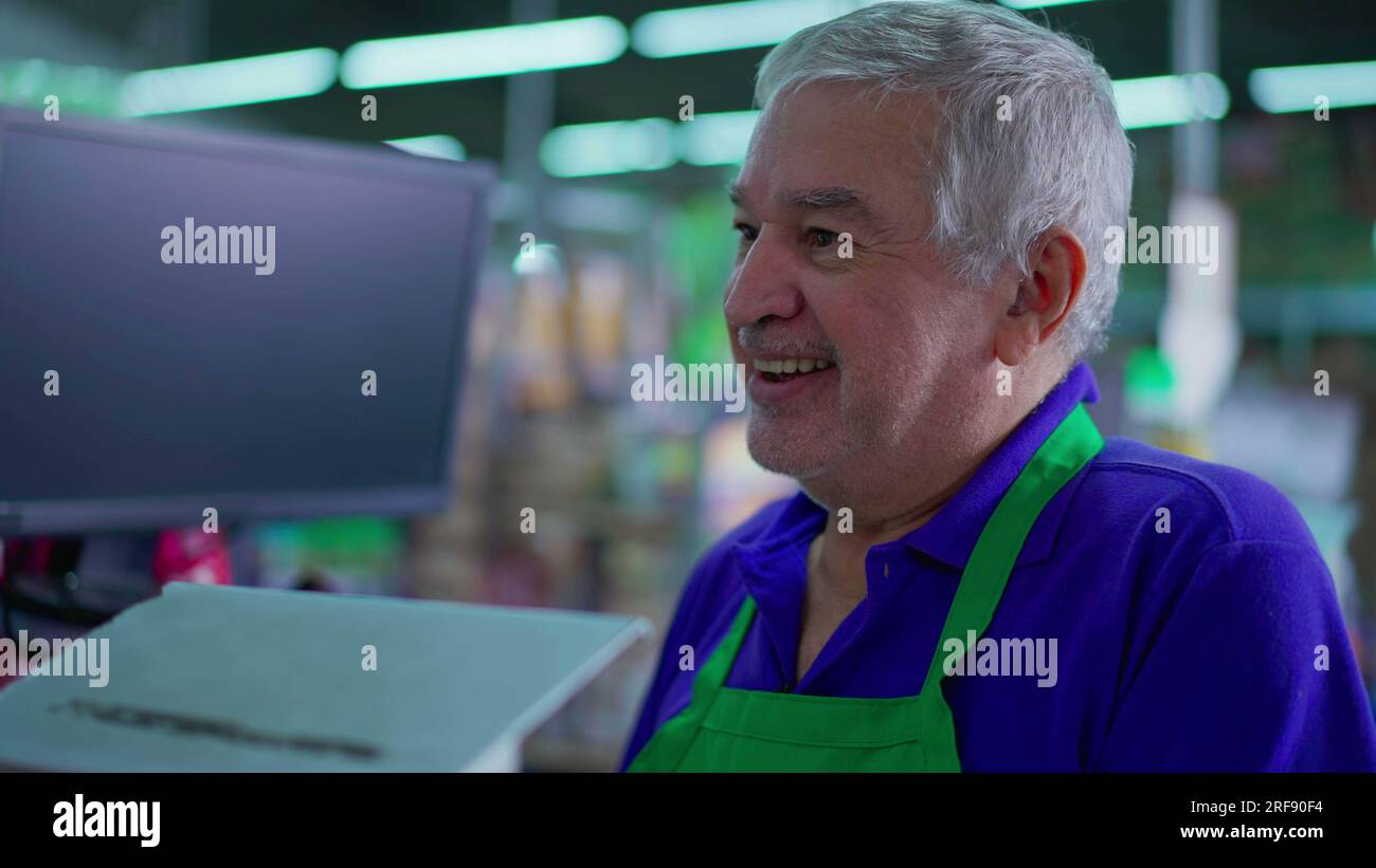 Happy senior employee of supermarket smiling at checkout cashier ...