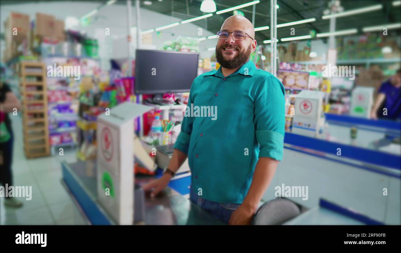 Happy supermarket employee standing at cashier checkout smiling at ...