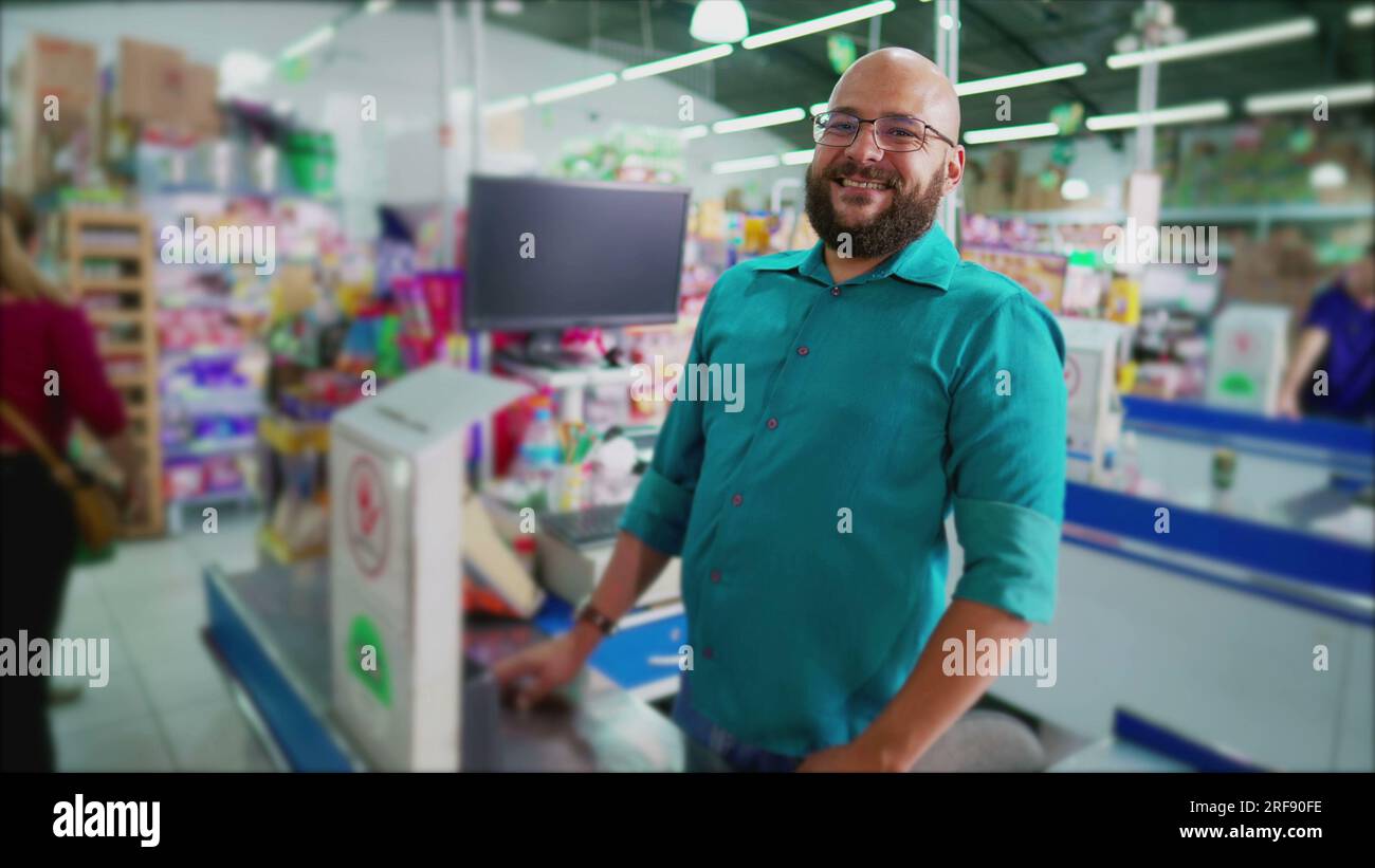 Happy supermarket employee standing at cashier checkout smiling at ...
