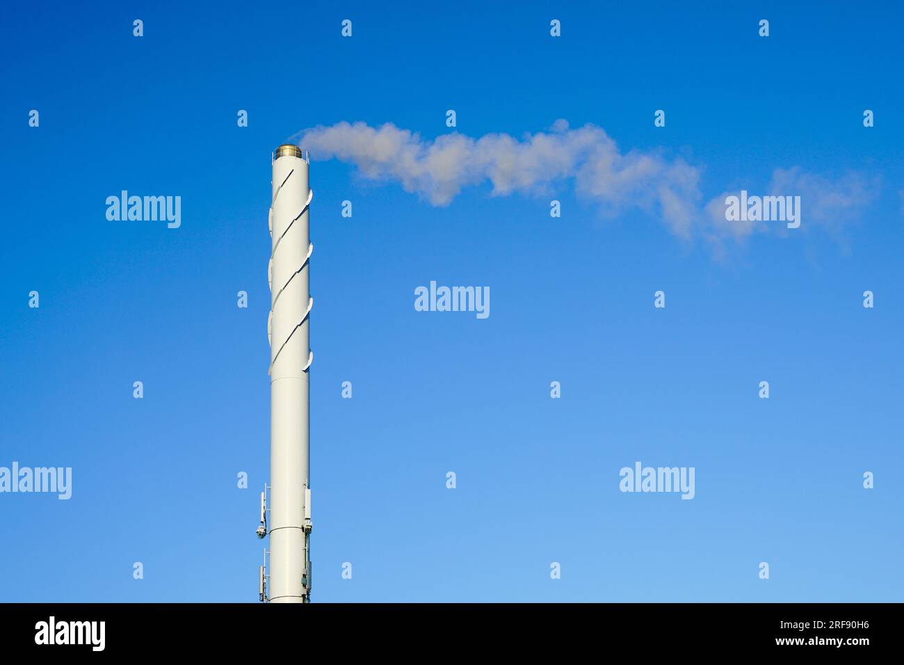 A tall white smoking chimney on a blue sky background, white steam ...