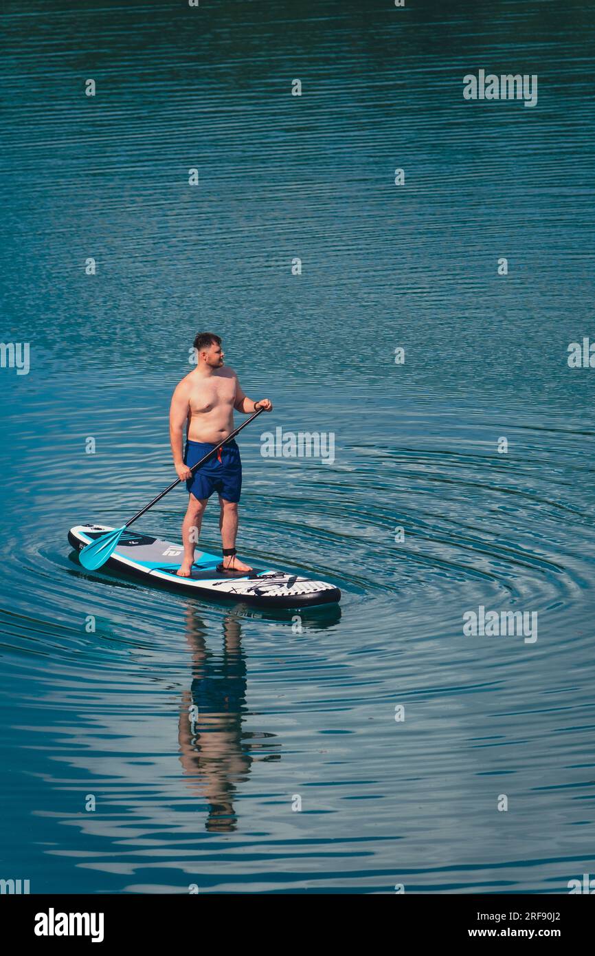 man balancing on supboard paddling on the middle of the lake water ...