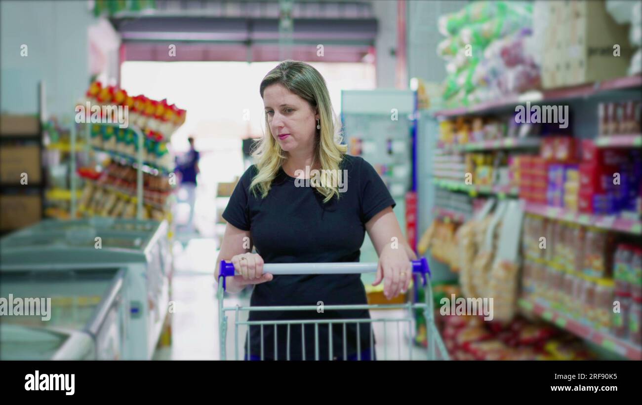 Female consumer walking in supermarket aisle browsing products on shelf ...