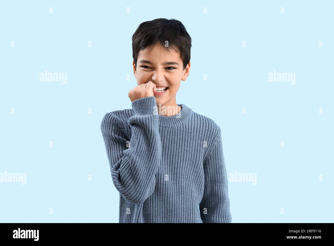 Angry little boy biting nails on blue background Stock Photo - Alamy