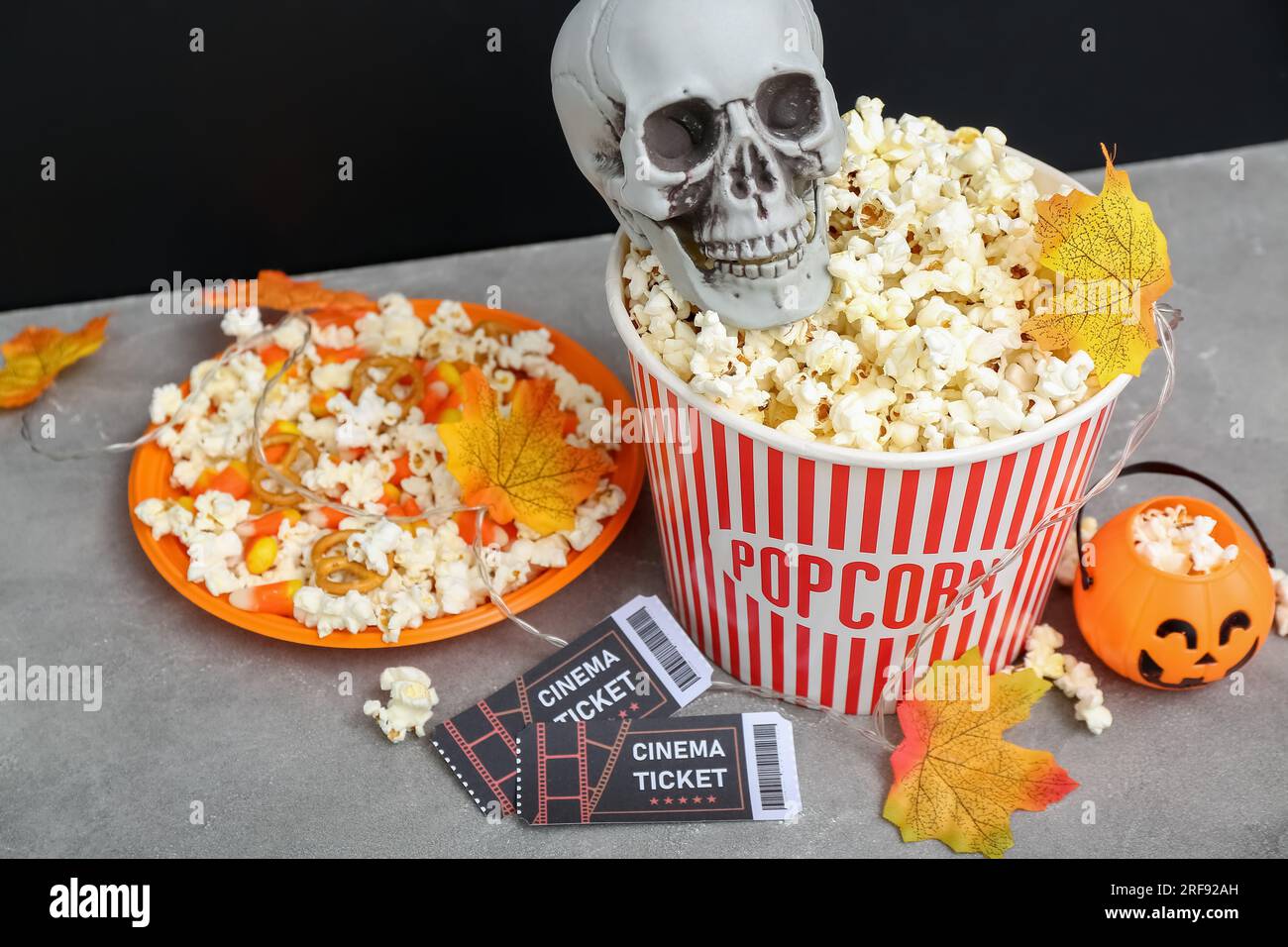 Bucket with tasty popcorn, skull and cinema tickets on grey table ...
