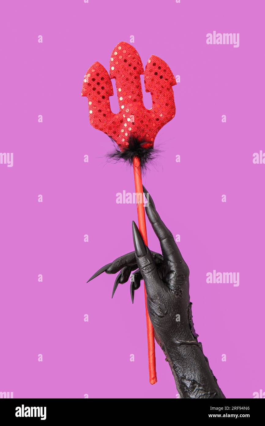 Hand of witch with red devil pitchfork on purple background. Halloween ...