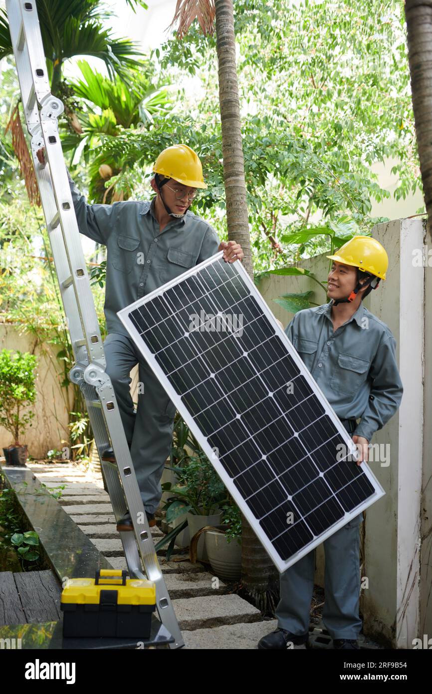 Contractor helping coworker to lift solar panel on roof Stock Photo - Alamy