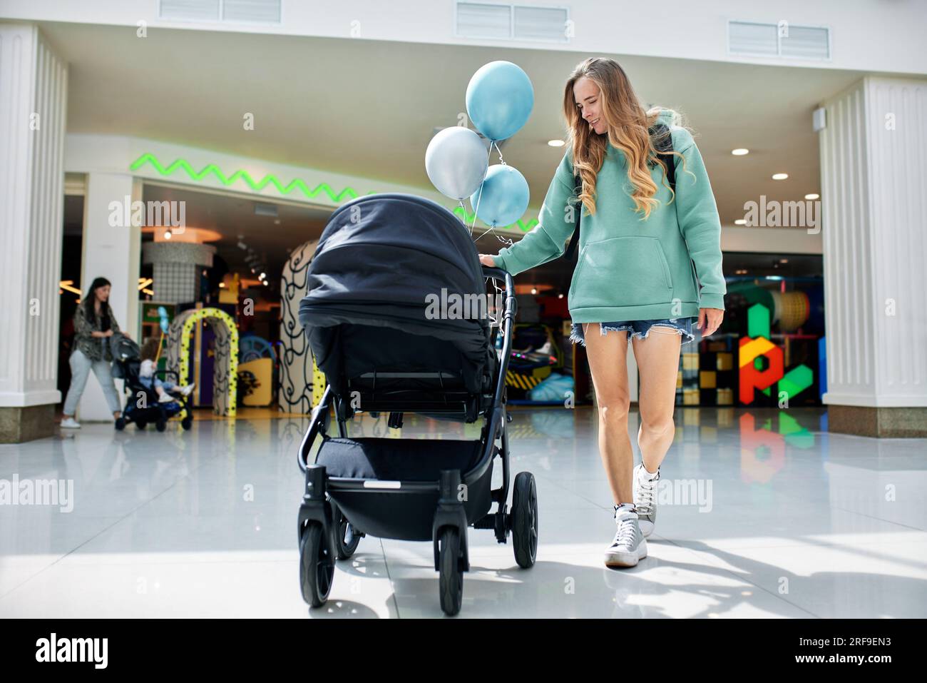 Happy mother with baby in stroller and colored balloons. Young pretty ...