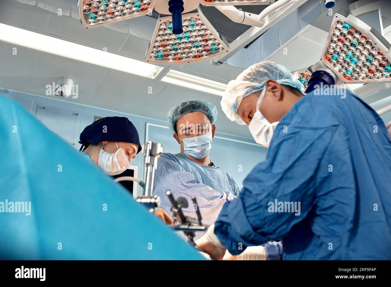Low angle view of surgeons leaned over patient during complex surgical ...