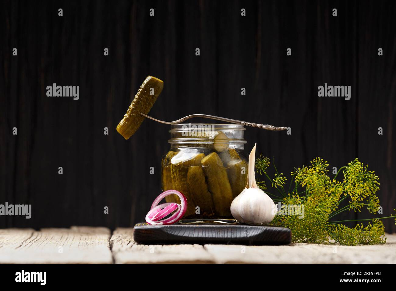 Canned cucumbers in an open jar, one gherkin on a vintage fork lies on ...